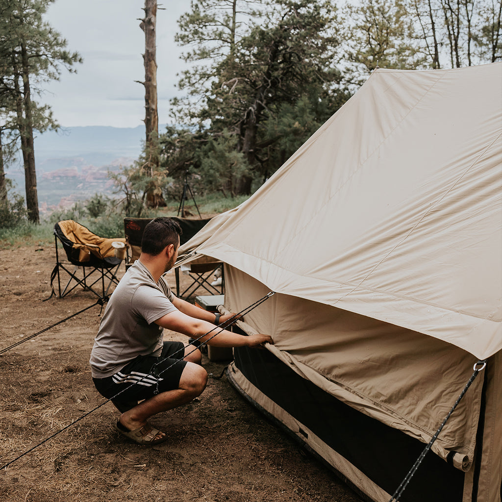 Rover scout tent placed in the forest while a man rolls up the sides to ...